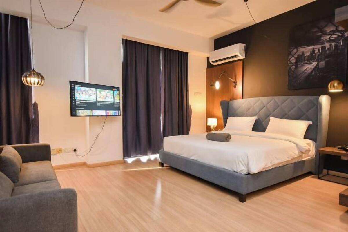 Quarto de hotel moderno com uma cama grande, televisão de tela plana, ventilador de teto e uma pintura com vista para a cidade.