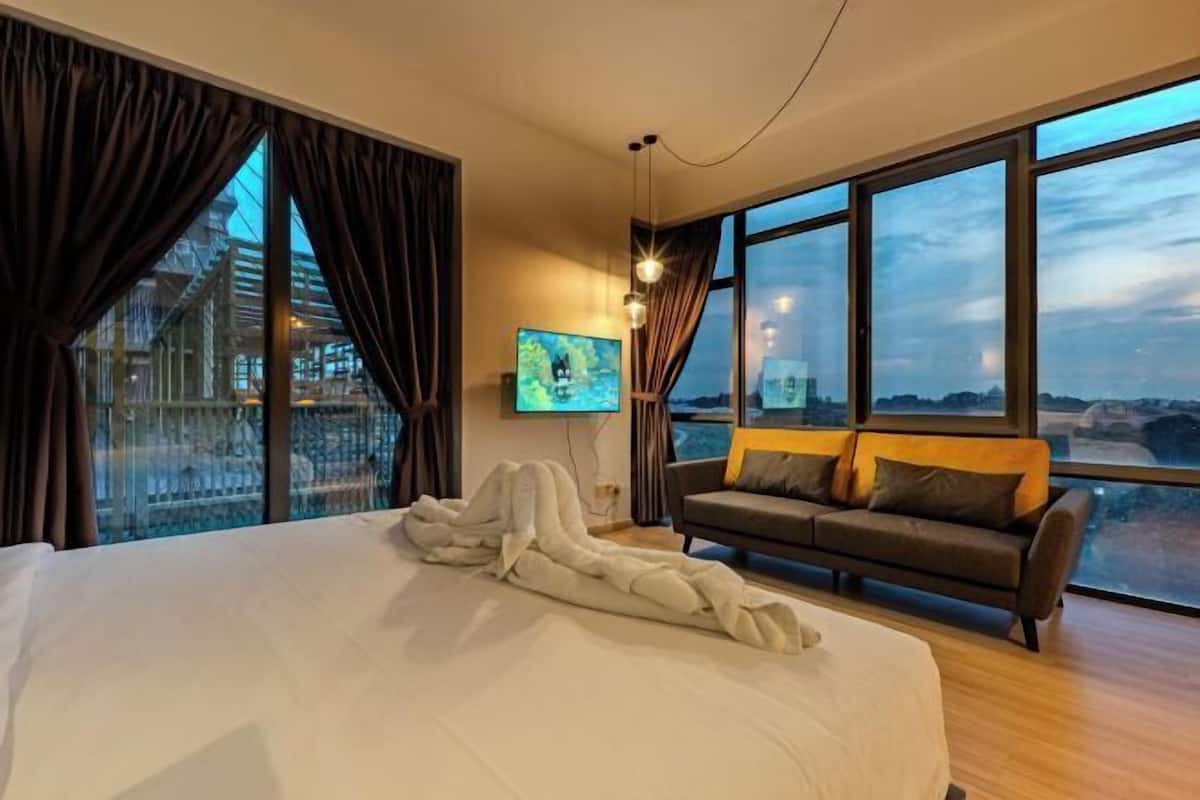 Quarto com cama grande, sofá, televisão e vista para a cidade.