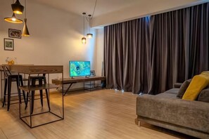 Uma sala de estar moderna com uma mesa de jantar de madeira, um sofá e uma televisão.