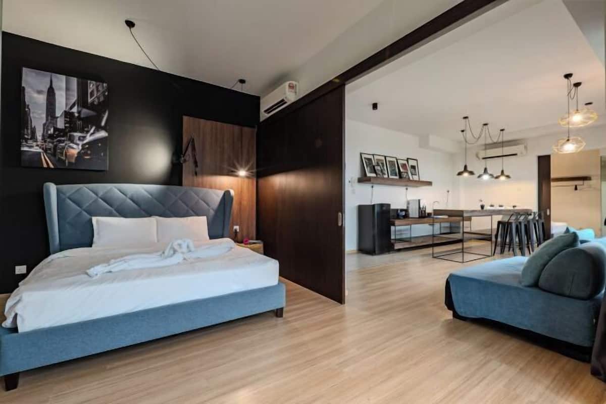 Quarto moderno com cama, uma pequena escrivaninha e uma kitchenette ao fundo.