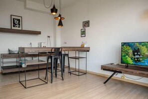 Cozinha moderna com bancada de madeira, banquetas, luminárias pendentes e uma TV de tela plana sobre um suporte de madeira.