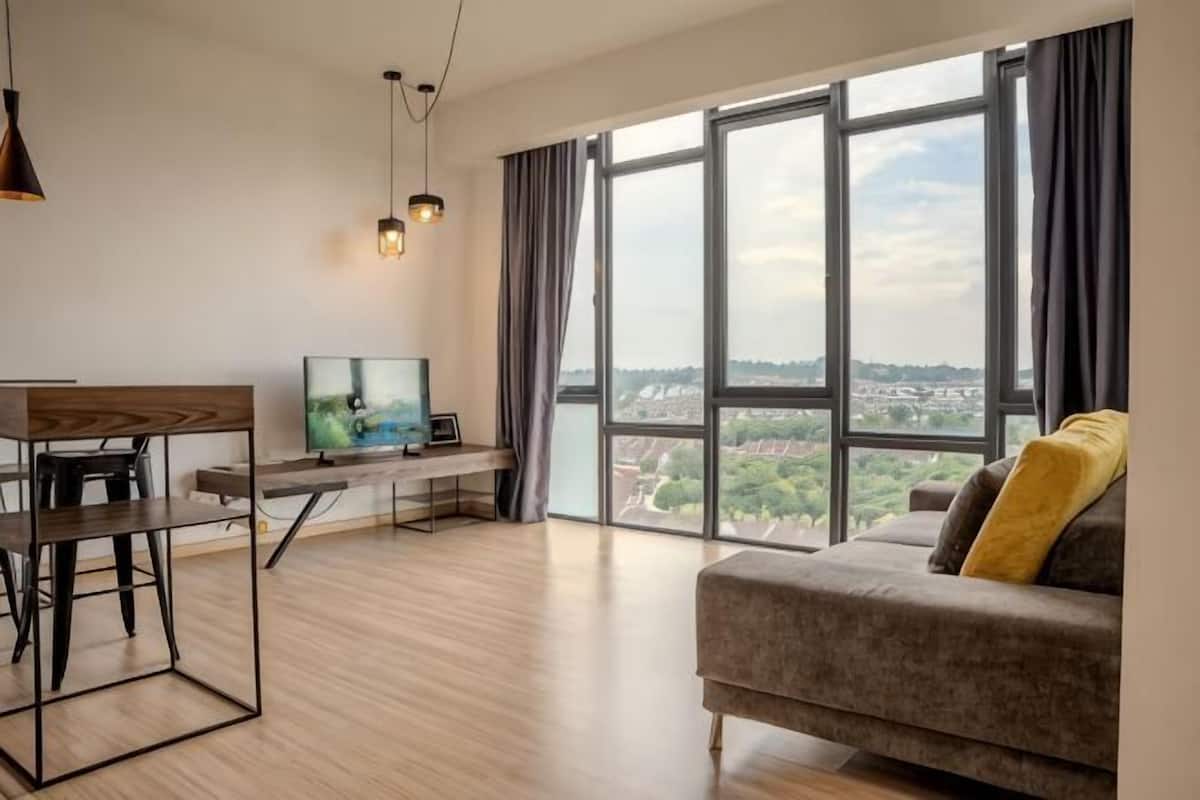 Uma sala de estar moderna com sofá, mesa de jantar, televisão e janelas amplas com vista para a cidade.