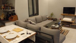 Uma sala de estar moderna com sofá, mesa de centro, televisão e área de jantar com mesa posta para dois.