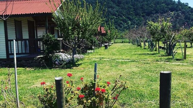 Um cenário rural com uma casa, um jardim cercado e uma paisagem acidentada.