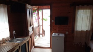 Interior em madeira com cozinha, geladeira e televisão fixada na parede.