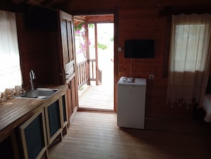 Interior em madeira com cozinha, geladeira e televisão fixada na parede.