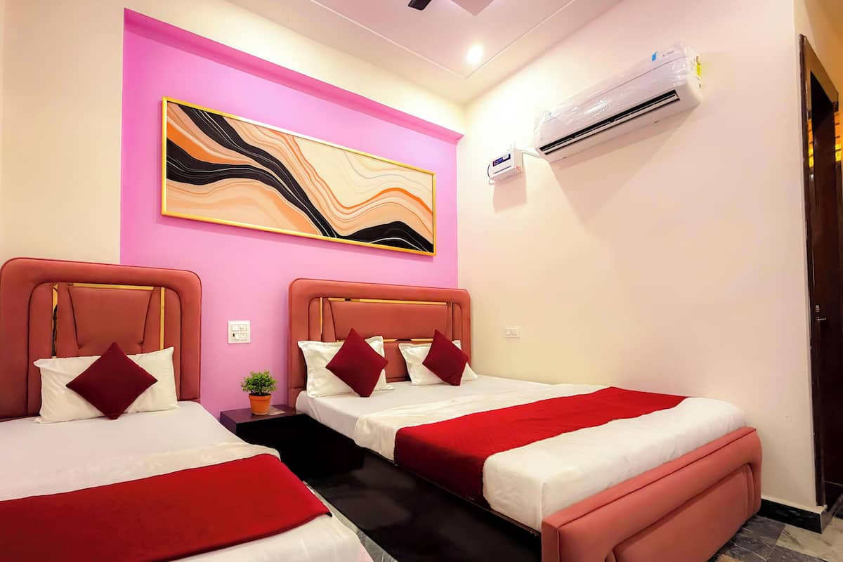 Quarto de hotel com duas camas, uma parede em tom rosa, uma pintura abstrata moderna, um aparelho de ar condicionado e uma pequena planta em vaso.