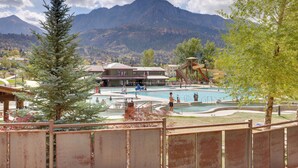 Uma área de piscina com montanhas ao fundo, um parquinho e um edifício com telhado vermelho.
