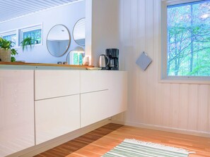 Cozinha moderna com armários brancos, cafeteira e janela com vista para árvores.