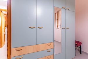 Guarda-roupa com várias gavetas e portas, um espelho e uma cadeira pequena com tecido vermelho.