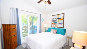 Um quarto com uma cama, um ventilador de teto, uma janela com cortinas, um relógio e um quadro na parede.