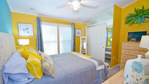 Um quarto com cama, cômoda, televisão e ventilador de teto.