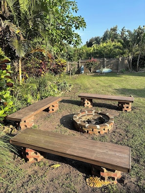 Um quintal com lareira de tijolos, bancos de madeira e um deck de madeira.