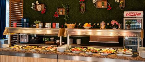 Um buffet com diversos tipos de comida, uma parede verde com decorações e uma placa em idioma estrangeiro.