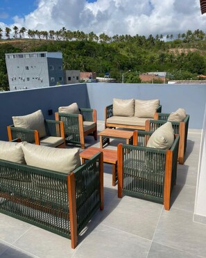 Terraço no telhado com móveis de exterior e vista para palmeiras e edifícios.