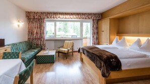 Um quarto com cama, sofá, poltrona, mesa e janela com cortinas.