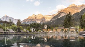 Um resort na montanha com uma piscina refletora, cadeiras de descanso e vista para as montanhas.