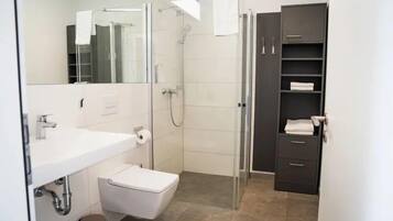 Uma casa de banho moderna com lavatório, sanita, chuveiro e um armário escuro com prateleiras.