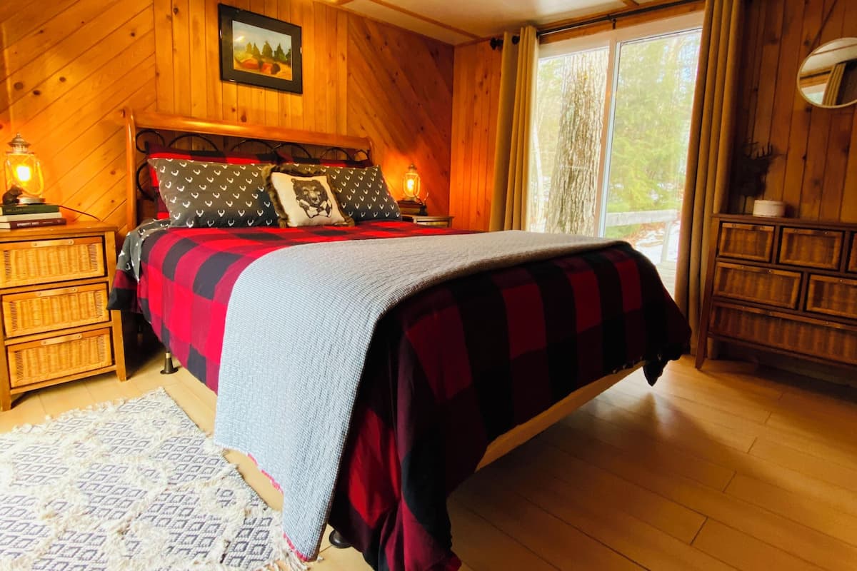 Quarto com painéis de madeira, uma cama, mesas de cabeceira, um tapete e uma janela.