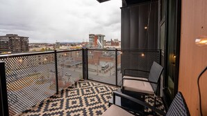 Uma varanda com piso estampado, uma mesa com cadeiras e vista para a paisagem urbana.