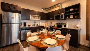 Uma cozinha moderna com armários escuros, uma geladeira de aço inoxidável, micro-ondas e uma mesa de jantar posta para seis pessoas.