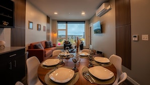 Uma área de jantar com mesa posta para quatro pessoas, um sofá e uma TV fixada na parede.