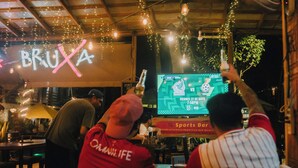 Um bar com letreiros de neon, um evento esportivo na televisão e luzes de corda.