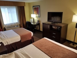 Quarto de hotel com duas camas, uma escrivaninha, uma televisão e um abajur.