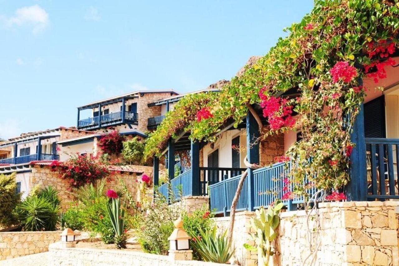 Um edifício de pedra tradicional com varanda, rodeado por vegetação exuberante e plantas floridas.