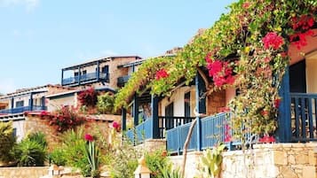 Um edifício de pedra tradicional com varanda, rodeado por vegetação exuberante e plantas floridas.