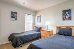 Quarto com duas camas, uma mesa de cabeceira, abajur e pôsteres de filmes na parede.