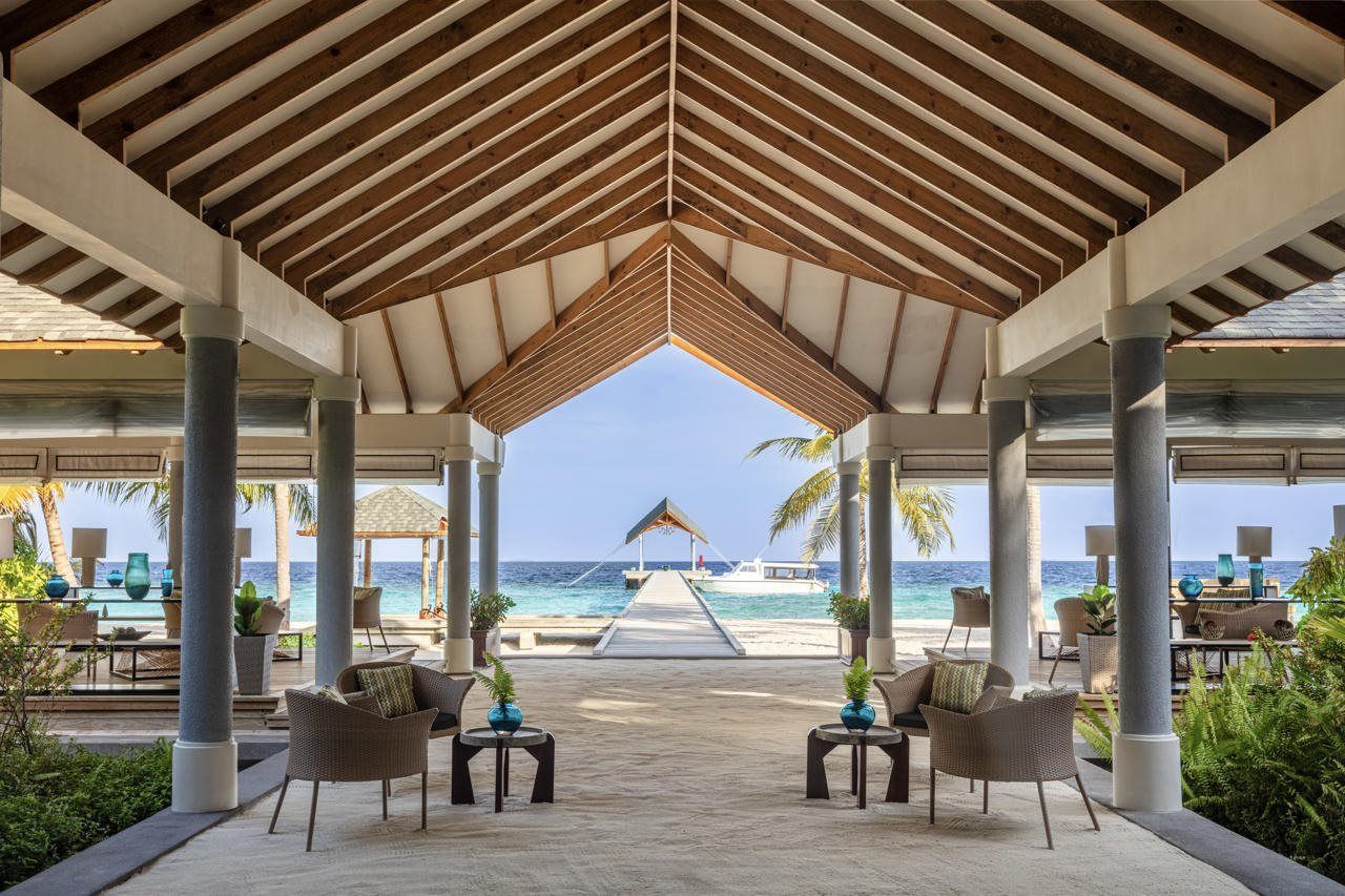 Uma área externa coberta com vista para o oceano, com cadeiras de lounge e mesas.