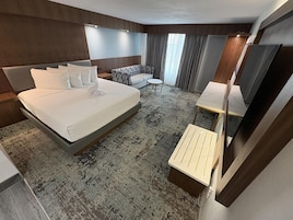 Quarto de hotel com uma cama grande, um sofá, uma mesinha, um espelho e uma televisão.