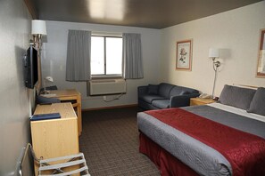 Quarto de hotel com cama, escrivaninha, cadeira, sofá, televisão e janela com cortinas.
