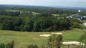 Um campo de golfe com bunkers de areia, um clube e colinas arborizadas ao redor.