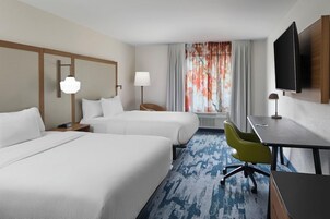 Quarto de hotel com duas camas, uma escrivaninha, uma cadeira, uma televisão e uma janela com cortinas.