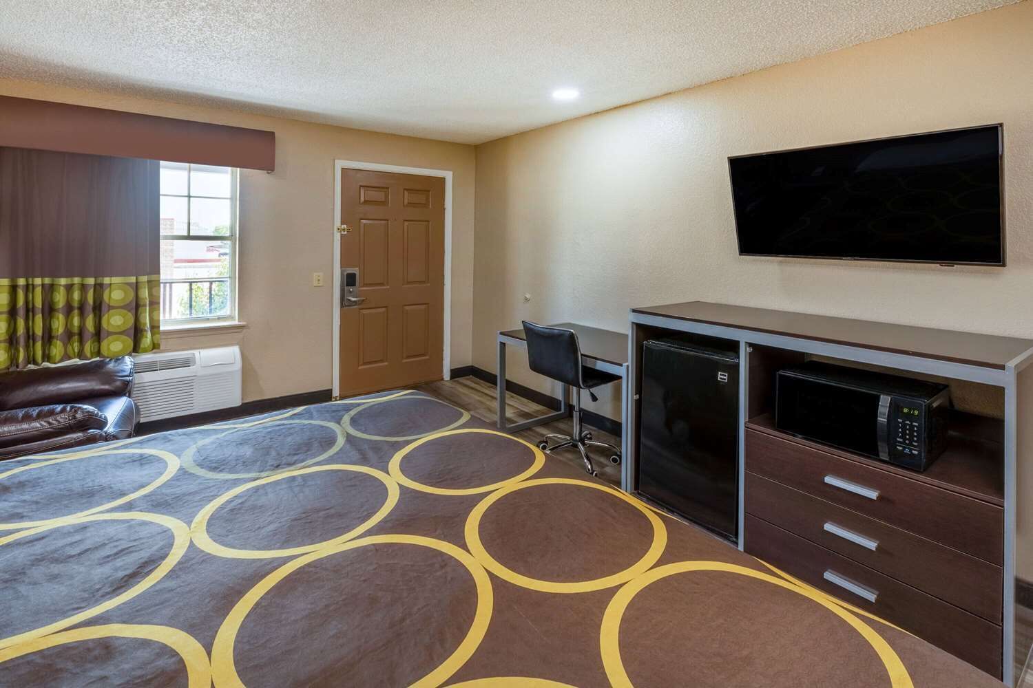 Quarto de hotel com uma cama, escrivaninha, televisão, frigorífico e micro-ondas.