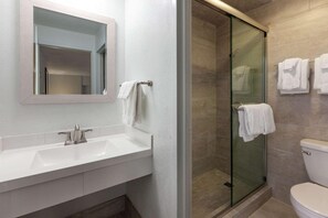 Casa de banho moderna com chuveiro em cabine de vidro, lavatório branco e sanita.