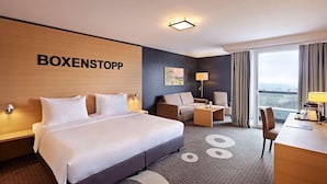 Quarto de hotel com uma cama grande, uma escrivaninha, uma cadeira, um sofá e vista para a cidade.