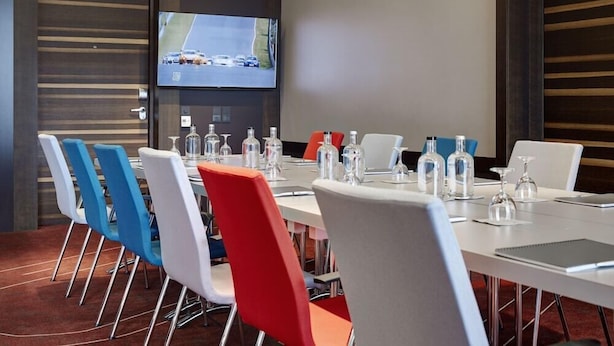 Uma sala de conferências com uma mesa comprida, várias cadeiras e uma televisão presa à parede.