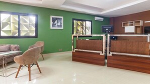 Uma área de recepção com balcão, cadeiras, sofá e televisão.