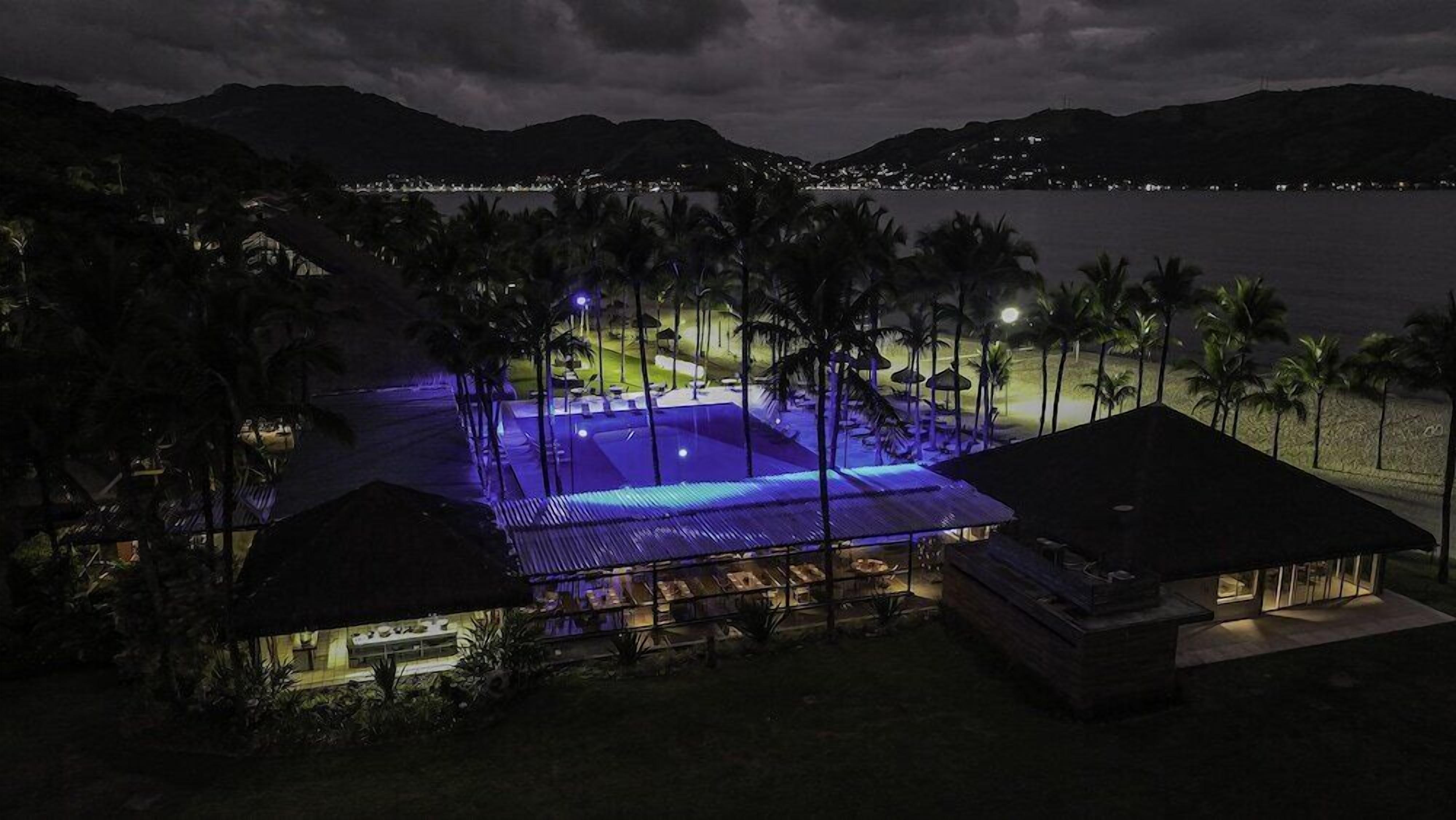 Um imóvel à beira-mar com piscina, palmeiras e vista para o mar.