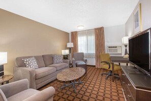 Quarto de hotel com sofá, poltronas, mesa de centro, televisão e aparelho de ar condicionado.