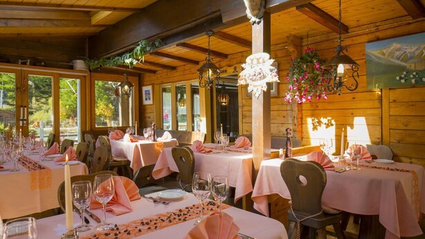 Restaurante com interiores em madeira, várias mesas preparadas para refeições e decorações florais penduradas.