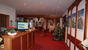 Um saguão de hotel com uma mesa de recepção, um pinheiro de Natal e obras de arte emolduradas nas paredes.