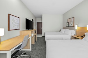 Quarto de hotel com escrivaninha, cadeira, duas camas, televisão e obras de arte nas paredes.