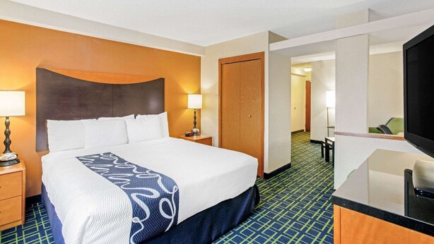 Quarto de hotel com cama, mesas de cabeceira, televisão e porta para um corredor.