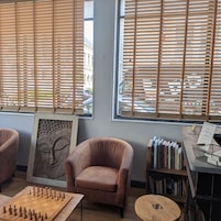 Quarto com um tabuleiro de xadrez, uma obra de arte emoldurada, uma cadeira e uma estante de livros.