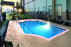 Piscina retangular com escada de metal, rodeada por um deck de concreto e cerca de metal preta.