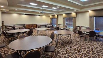 Sala de conferências com várias mesas e cadeiras, piso coberto por carpete e tela de projeção.
